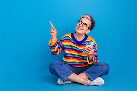 예쁜 아가씨의 전체 길이 사진은 바닥에 앉아서 스마트 폰을 보면 파란색 배경에 고립 된 손가락 빈 공간을 나타냅니다 Brand