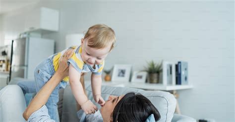 백인 사랑하는 엄마는 거실의 소파에서 아기 아이와 놀고 있습니다 행복한 가족 매력적인 아름다운 돌보는 젊은 어머니 들어 올리는 유아 아들이 집에서 아침에 비행기 게임을