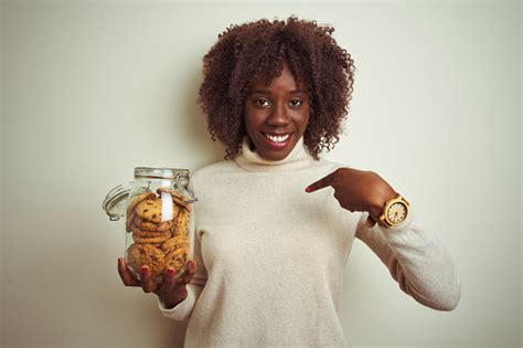 자신에게 손가락을 가리키는 깜짝 얼굴과 고립 된 흰색 배경 위에 서 쿠키의 항아리를 들고 젊은 아프리카 아프로 여자 가리키기에 대한 스톡 사진 및 기타 이미지 Istock