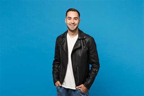 블랙 가죽 자 켓 흰색 T 셔츠에 잘생긴 세련 된 젊은 수염 남자 블루 벽 배경 스튜디오 초상화에 고립 된 카메라를 찾고 사람들은 진심으로 감정 라이프 스타일 개념입니다