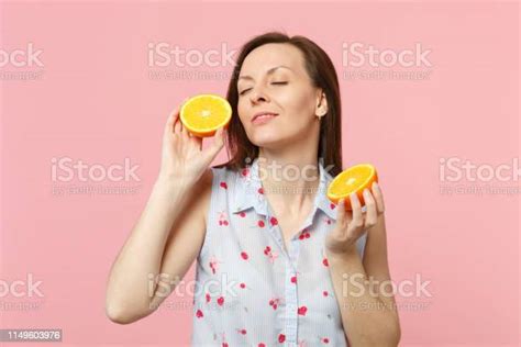 여름 옷에 예쁜 젊은 여성이 분홍색 파스텔 배경에 고립 된 신선한 잘 익은 오렌지 과일의 Halfs를 들고 눈을 유지 사람들은