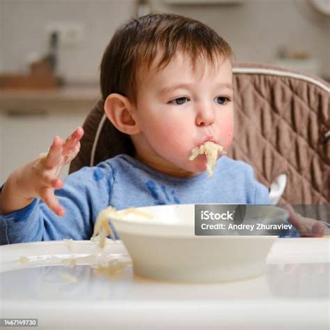 재미있는 아이가 부엌 의자에 앉아있는 동안 입이 가득 찬 강판 사과를 먹고 있습니다 배고픈 아기는 입에 음식을 밀어 넣고 유머를