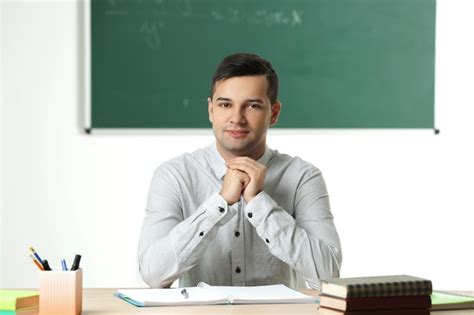 Premium Photo Handsome Young Teacher Sitting At Table In Classroom