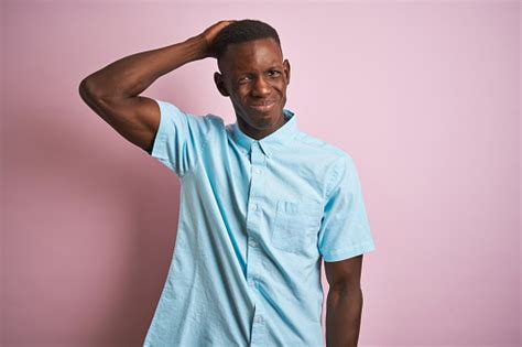 고립 된 분홍색 배경 위에 서있는 파란색 캐주얼 셔츠를 입은 아프리카 계 미국인 남성이 혼란스럽고 질문에 대해 궁금해합니다 의심의 여지가 머리에 손으로 생각 펜시브 개념
