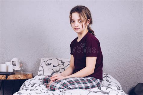 A Teenage Girl In Pajamas Is Sitting On The Bed And Smiling Stock
