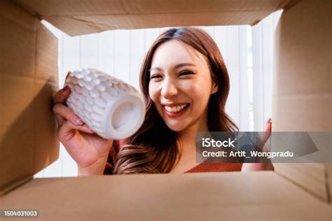 상자 안에서 바라보는 미소 짓는 여자는 꽃병을 들고 꽃병을 들고 앉아 온라인 상점 주문이 담긴 골판지 상자를 여는 행복한 고객을 만족시켰습니다 실내에 대한 스톡 사진 및