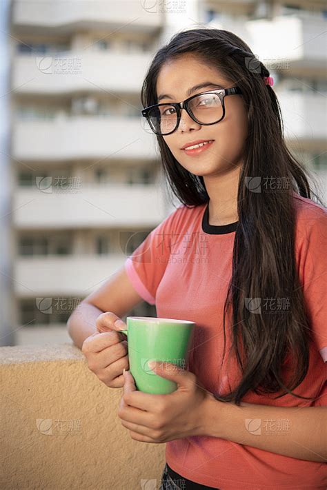 漂亮的年轻女子站在阳台上拿着一个咖啡杯看着镜头