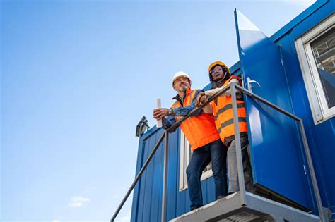 건설 현장의 이동식 사무실 앞에 서서 건설 현장을 바라보고 있는 현장 관리자와 건설 노동자 20 24세에 대한 스톡 사진 및