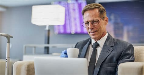 라텍스 장갑과 안경을 쓴 쾌활한 우아한 남성이 커피를 마시고 비행 전에 노트북을 사용하고 있다 사진 Unsplash의 여행 가방 이미지