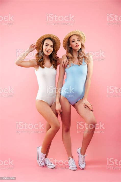 분홍색 배경에 고립 된 사랑스러운 표정과 미소로 포즈를 취하는 화려한 원피스 수영복과 밀짚 모자를 입은 멋진 소녀 20 대의 전체 길이 사진 2명에 대한 스톡 사진 및 기타