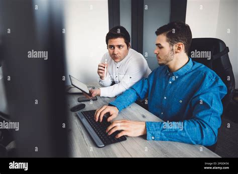 Two Young Caucasian Programmers Working On Desktop Computers In The Office Developing A New