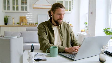 دانلود فوتیج ویدیویی ردی که پشت میز در اتاق نشیمن نشسته است و با لپ تاپ کار می کند استوک فوتیج