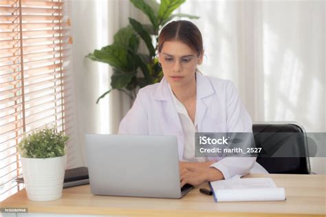 노트북 컴퓨터를 사용하고 클리닉에서 진단을위한 환자에 관한 문서 종이를보고있는 젊은 여성 의사 클립 보드에서 문서를 읽고 일하는