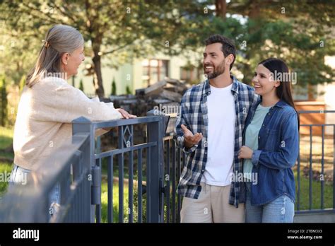 Friendly Relationship With Neighbours Happy Young Couple Talking To Senior Woman Near Fence