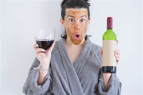 미용 얼굴 마스크를 착용 하는 아름 다운 여자 로 스킨 케어 치료 마시는 유리 와인의 충격에 충격 두려움과 두려움 표정으로 흥분 갈색 머리에 대한 스톡 사진 및 기타 이미지