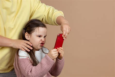 여자의 손 베이지 색 배경에서 멀리 스마트 폰을 복용 부모의 초상화 화가 난 딸은 꽉 전화를 잡고 저항합니다 어린이 의 전화 중독 예방의 개념 Nomophobia 몰수에