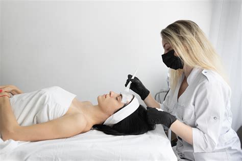 미용사는 스파에서 여성의 얼굴에 효소 박리를 적용합니다 브러시가 있는 흰색 마스크를 적용합니다 현대적인 뷰티 살롱에서 화장품