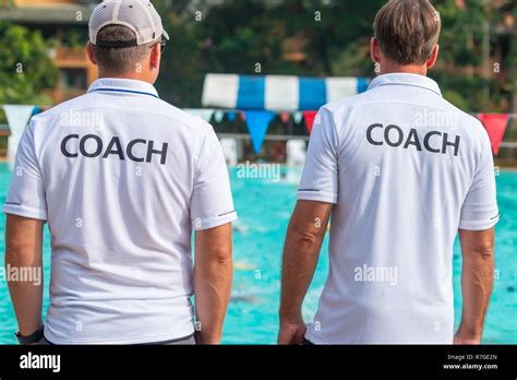 Back View Of Swimming Coaches Wearing Coach Shirt Working Together At