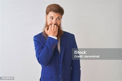 젊은 빨간 머리 아일랜드어 사업가 는 입물고 손톱에 손을 긴장 찾고 고립 된 흰색 배경 위에 서 양복을 입고 불안 문제 감정에 대한 스톡 사진 및 기타 이미지 Istock