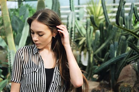 모자와 용 설 란과 선인장 식물 근처 온실 내부 햇빛 Basking 스트라이프 블라우스를 입고 긴 머리를 가진 젊은 유행 백인 여자 걷기에 대한 스톡 사진 및 기타 이미지