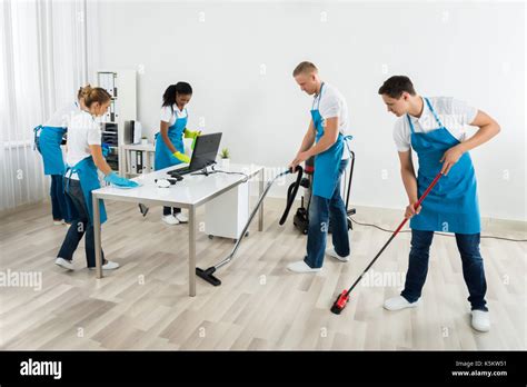 Group Of Male And Female Janitors In Uniform Cleaning The Office Stock