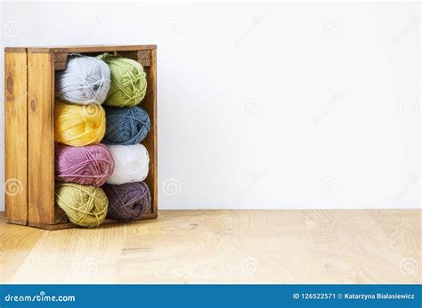 close up of a colorful yarn stack in a wooden crate by a white wall and copy space real photo
