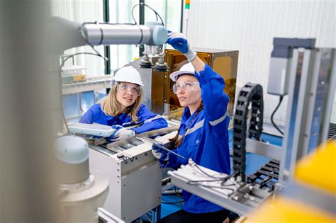 두 명의 예쁜 전문 기술자 또는 엔지니어 여성이 앉아서 공장 작업장에서 로봇 기계로 시스템 사용 컨트롤러와 Ipad를 확인하는