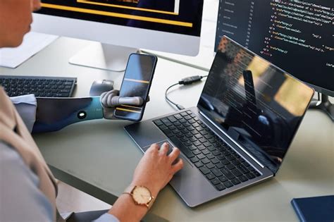 Premium Photo Software Developer Holding Smartphone In Bionic Hand When Programming In Laptop