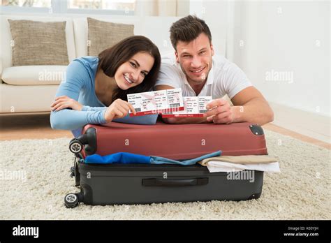 Portrait Of Happy Young Couple Packing Luggage Showing Boarding Pass