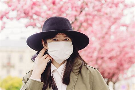 야외에서 걷는 동안 의료 용 마스크를 착용한 젊은 여성 바이러스 발생 시 분홍색 나무를 피는 배경에 도시 거리에 서 얼굴