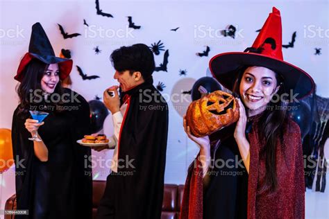 조각 된 호박을 들고 할로윈을 축하하는 의상을 입은 젊은 아시아 여성 할로윈 의상을 입은 그룹 젊은이들의 행복한 친구들을 축하하며 무서운 얼굴을 하며 집에서 파티를 즐기고