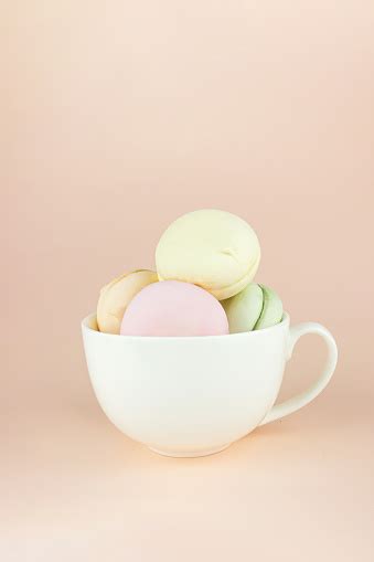 프렌치 머랭 쿠키 마시멜로는 파스텔 베이지 색 배경에 도자기 화이트 커피 컵 머그잔을 입은 마카롱처럼 보입니다 귀여운에 대한