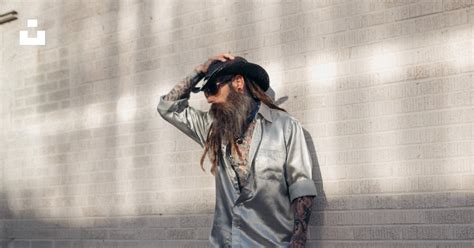 긴 머리와 벽에 기대어 있는 수염을 가진 남자 사진 Unsplash의 무료 의류 이미지