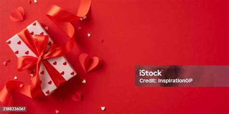 빨간 리본으로 아름답게 포장된 선물 상자가 작은 하트로 장식된 빨간 표면 위에 놓여 사랑과 축하의 감정을 불러일으킵니다 빨강에