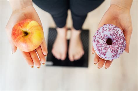 다이어트입니다 여 자가 측정 몸 무게에 무게 규모 들고 도넛 그리고 애플 과자는 건강에 해로운 정크 푸드 패스트 푸드 과체중에