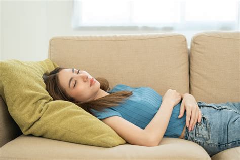 아시아의 백인 여자는 거실의 편안한 소파에 누워 있다 아시아 여성은 잠이 들고 낮잠을 잔다 지친 젊은 여자 아늑한 소파 현대적인 거실 내부의 신선한 공기 레저 아름다운
