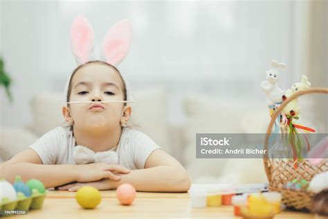 그녀의 머리에 토끼 귀에 재미 장난 어린 소녀 테이블에 앉아 부활절 작은 것들에 둘러싸여 윗입술과 코 사이에 페인트 브러시를 들고 가정 생활에 대한 스톡 사진 및 기타