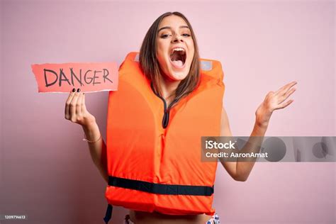 젊은 아름다운 갈색 머리 여자 위험 메시지와 종이를 들고 구명 조끼를 입고 매우 행복하고 흥분 큰 미소와 함께 비명을 지르는 승리를 축하하는 우승자 표정 갈색 머리에 대한