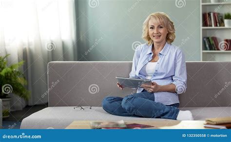 Красивая зрелая женщина сидя на кресле и ходить по магазинам онлайн смотрящ в камеру Стоковое