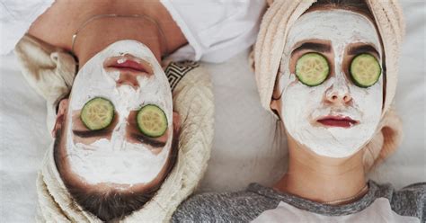 거꾸로 누워 얼굴에 신선한 오이 링과 흰색 마스크를 사용하여 피부 관리의 개념 두 여자 자매는 침실에서 주말을 보낸다 사진