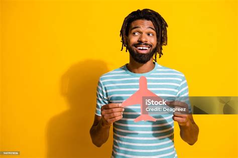 선명한 노란색 배경에 고립 된 빈 공간을 바라 보는 분홍색 비행기 컷 아웃을 들고있는 꿈꾸는 아프리카 계 미국인 남자의 사진 초상화 T 셔츠에 대한 스톡 사진 및 기타