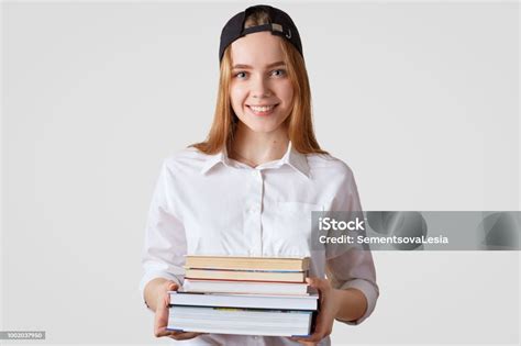 예쁜 대학생 긍정적인 Expreession 착용 세련 된 모자와 셔츠 보유도 서의 더미 도서관에가 흰색 배경에 고립 된 시험에 대 한 준비 합니다 사람과 공부 개념 교육에