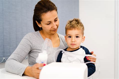 여자 어머니는 증기 증기 흡입기 분무기 마스크 흡입을 사용하여 그녀의 작은 아들 소년 아이를 집 이나 병원 의료 절차 약치료 치료 천식 폐렴 기관지염 기침 아픈 2 3 살에