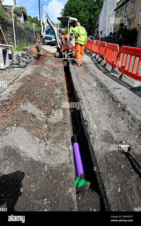 Workmen Installing Ducting For Fibre Optic Cable In Trench Cut In Road With Vibrating Whacker