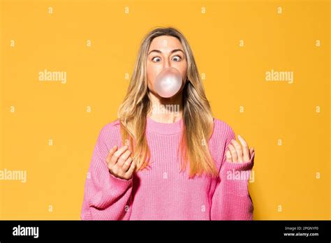 Woman Blowing Bubble From Chewing Gum Against Yellow Background Stock