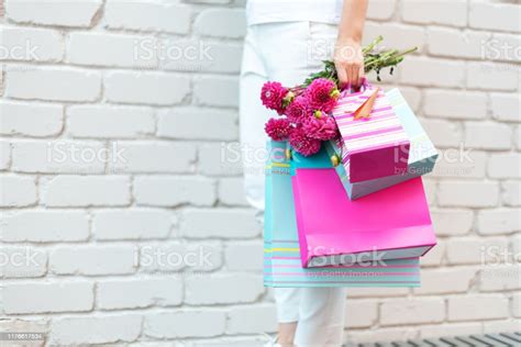 벽돌 배경에 꽃과 쇼핑 백을 들고 여성의 손 여자의 날 발렌타인 데이 생일 파티를위한 준비 공간을 복사합니다 종이 선물 가방 의 무리 가방에 대한 스톡 사진 및 기타 이미지