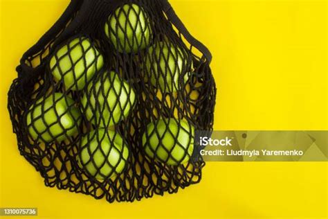 비닐 봉지 개념이 없습니다 노란색 배경에 녹색 사과가있는 메쉬 쇼핑 블랙 백 맨 위 보기입니다 공간을 복사합니다 0에 대한 스톡