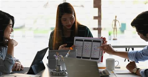 Ux Ui 개발로 일하는 아름다운 여성은 사무 장비가 있는 현대적인 회의 테이블에서 동료들에게 프로젝트를 보여줍니다 사진