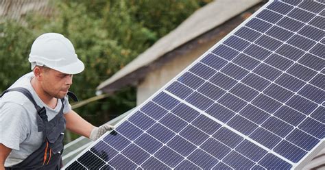 남자 기술자는 집 지붕에 태양광 모듈을 들고 있다 헬멧을 쓴 전기 기사가 야외에 태양 전지판 시스템을 설치하고 있다 대체 및