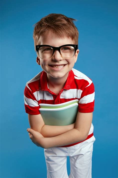 Smart Boy In Nerdy Glasses And Red Striped Shirt Looking Straight At Camera While Holding